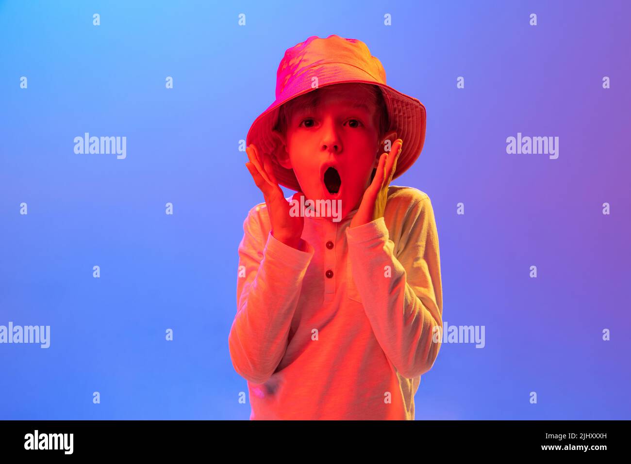 Shocked little boy, kid in pink panama hat isolated on gradient blue ...