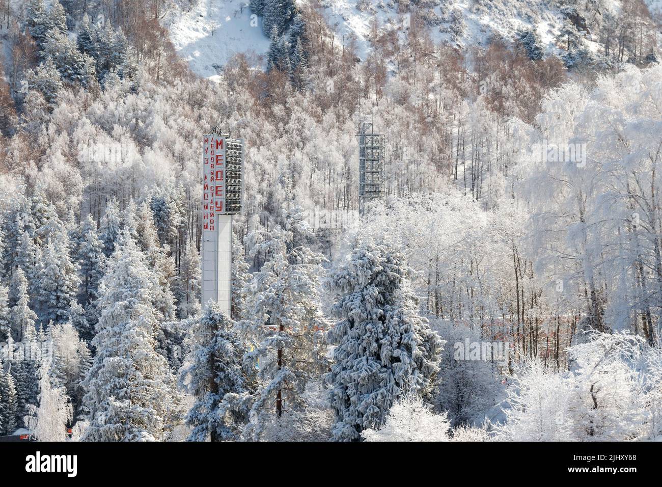Stele with the logo of the Medeo ice arena among the snow-covered trees ...