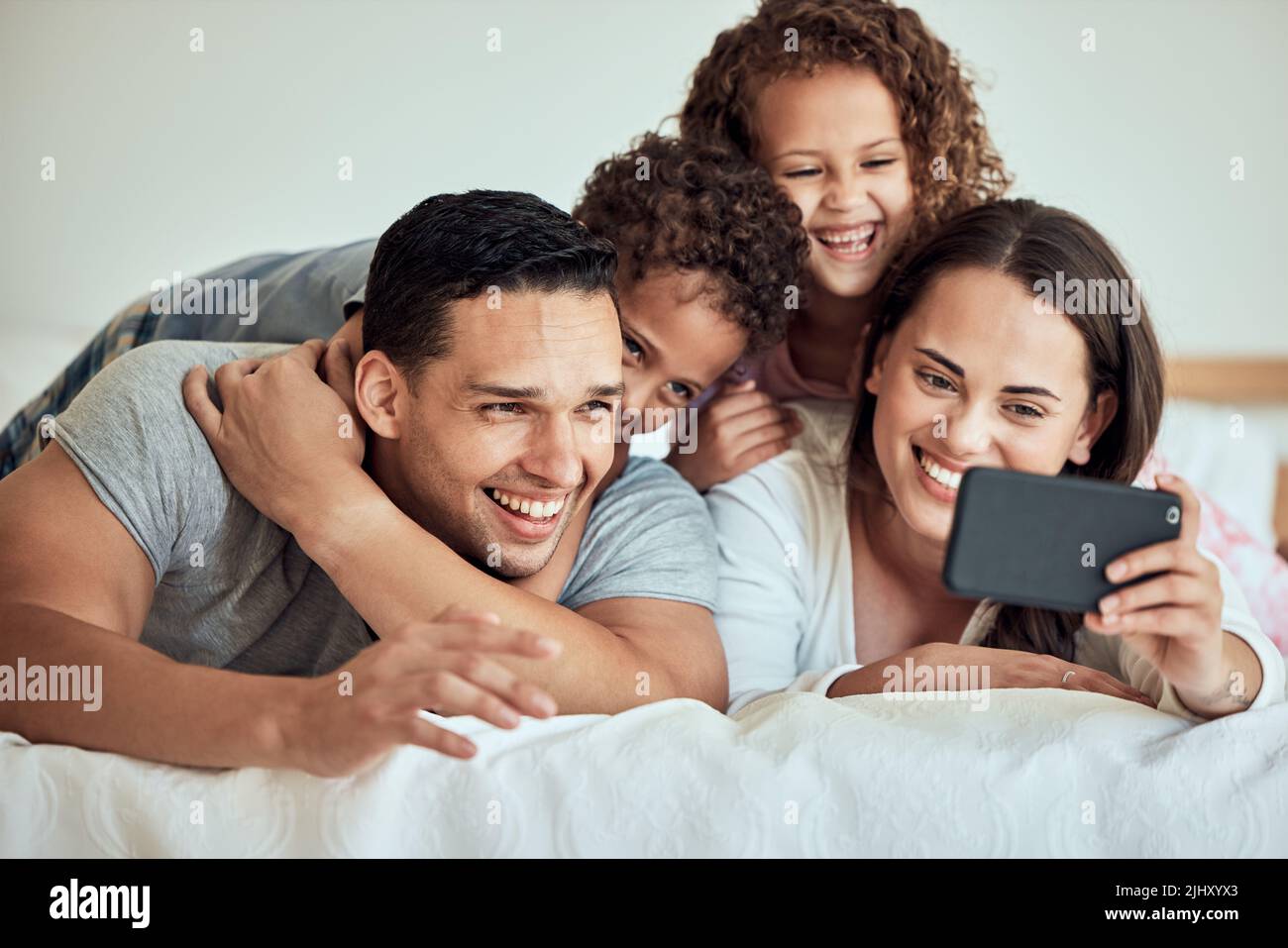 Family taking a selfie with a cellphone in bed. Happy hispanic family ...