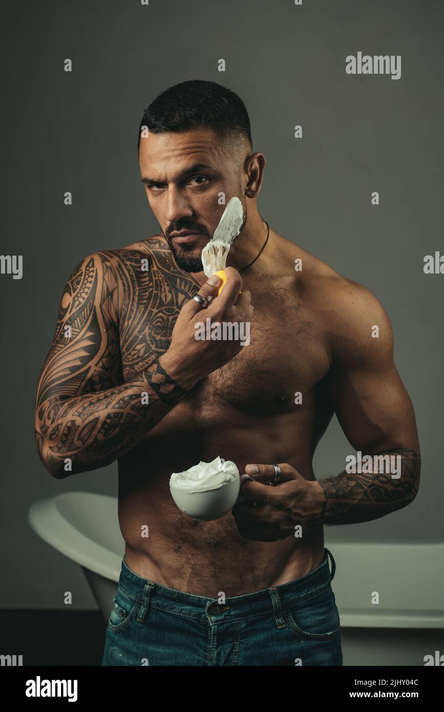 Bearded handsome tattooed man apply a shaving foam at his face. Bath ...