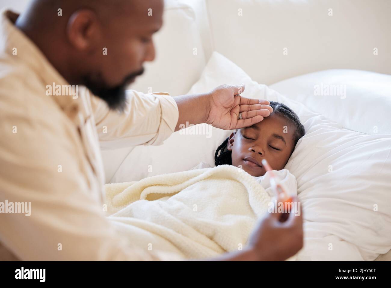 African american father checking his sick daughters temperature while taking care of her at home ...