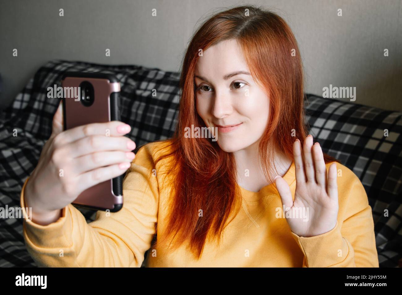 Young red-haired woman communicates online using smartphone. Concept of ...