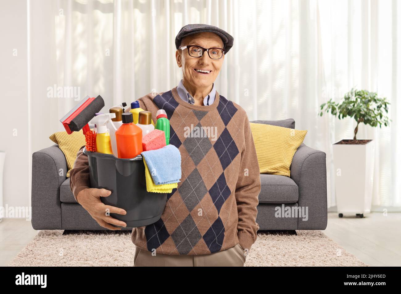 Elderly man holding a bucket with cleaning supplies and standing inside ...