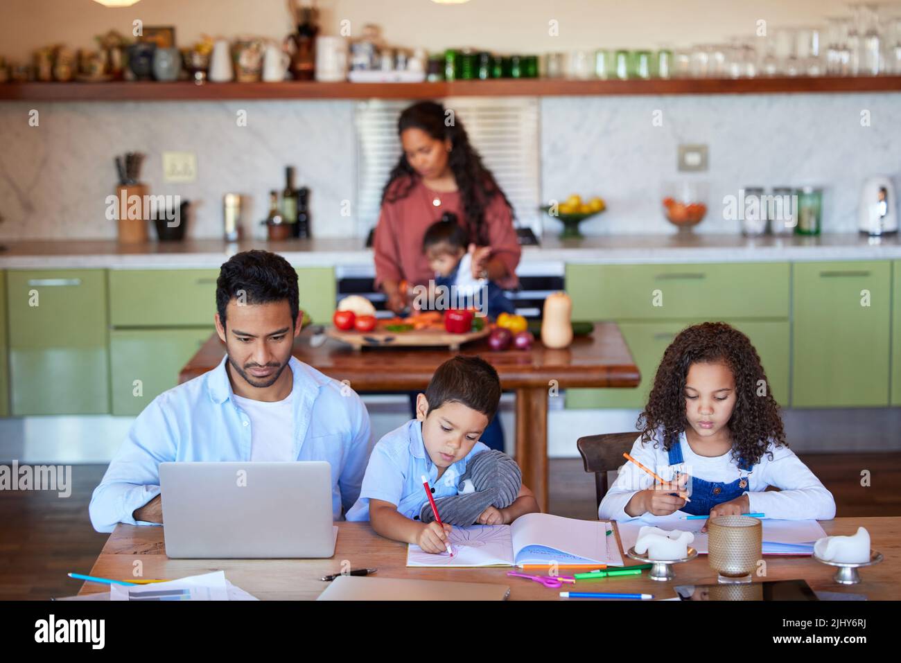 Young dad working on laptop while kids draw and do homework. Father and ...