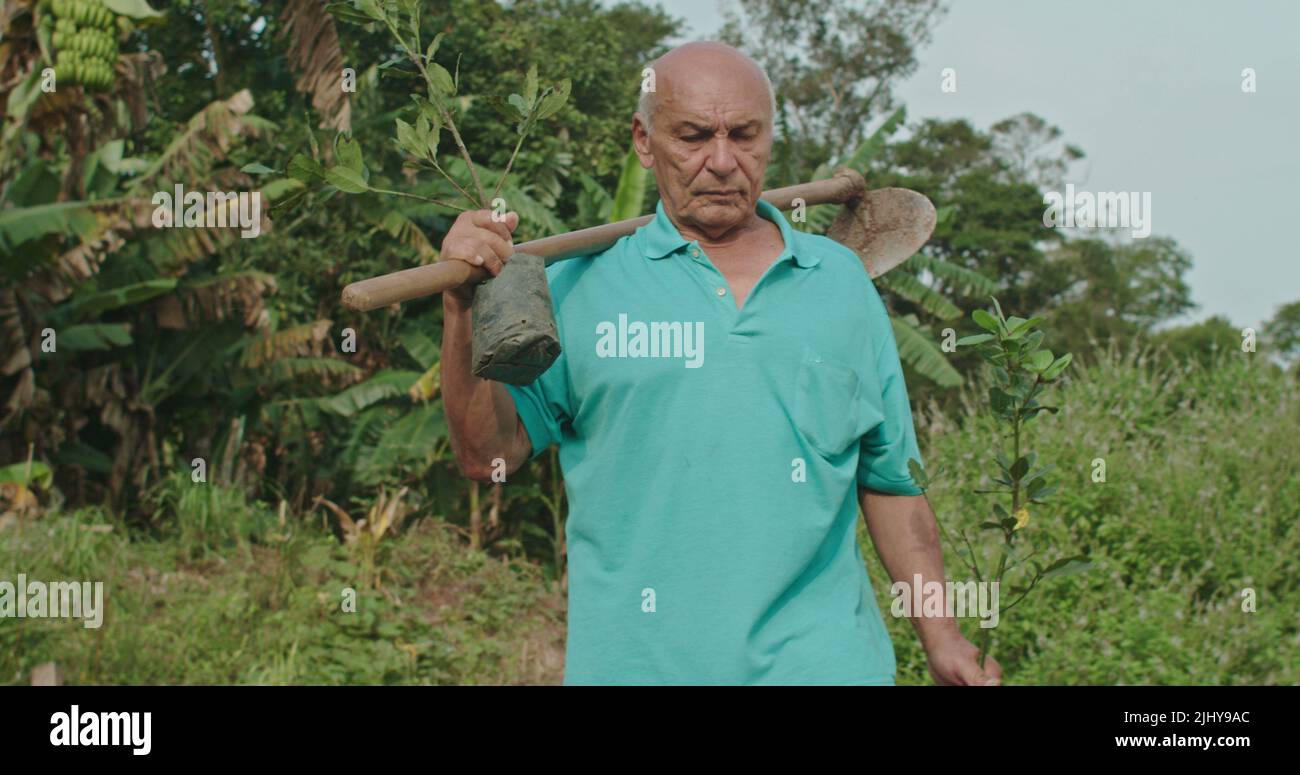 A mature hispanic man carrying farming equipment and two potting ...
