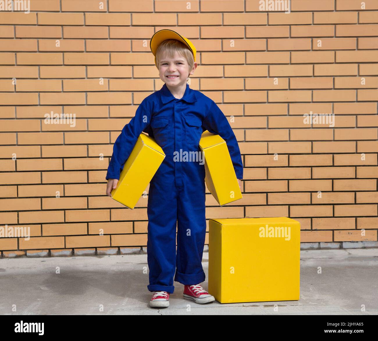 cute boy of 6 years old in blue overalls - uniform stands near brick ...