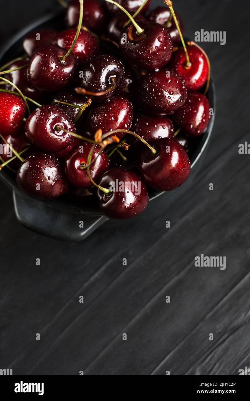 Fresh sweet cherries with water drops in bowl on dark rock table. Copy ...