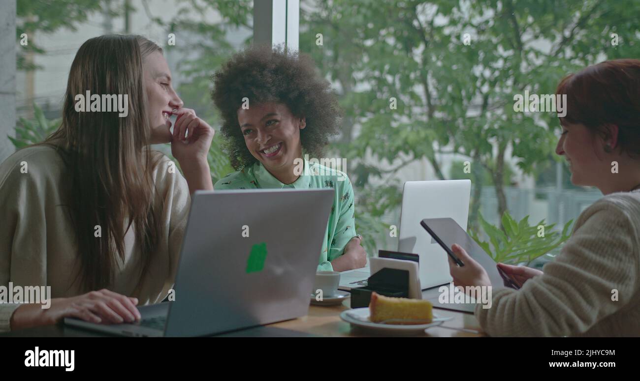 Group of three women talking at coffee shop. Friend sharing story with colleagues laughing and ...