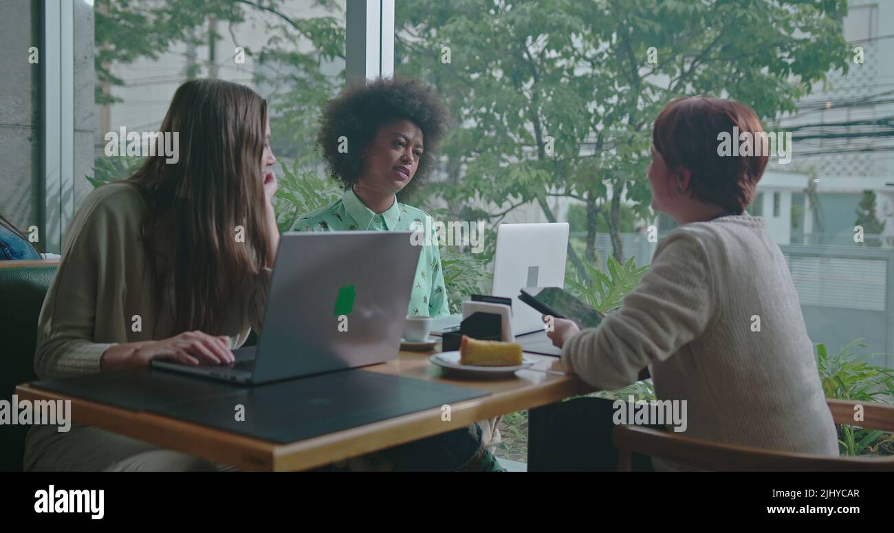 Friends sitting at table inside coffee shop talking. Three female ...