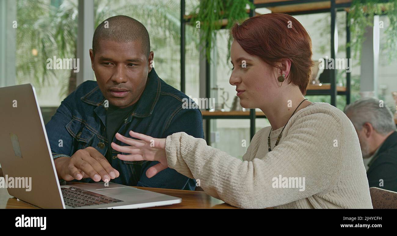 Two diverse young people in front of laptop at coffee shop. Woman ...