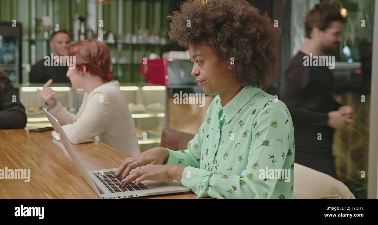 A happy black woman using laptop at coffee shop. One African American ...