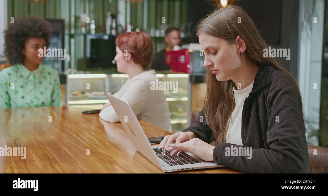 A focused young woman using laptop sitting at coffee shop. Girl looking ...