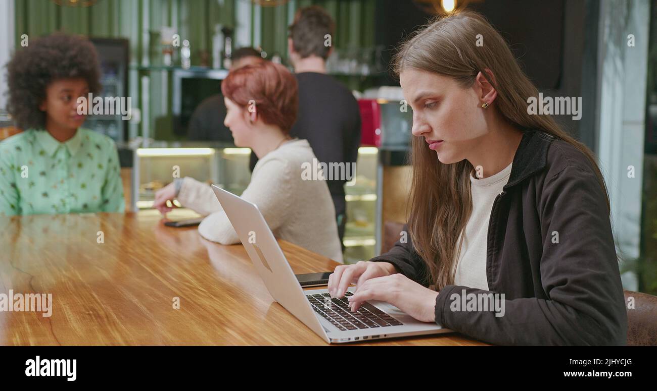 A focused young woman using laptop sitting at coffee shop. Girl looking ...