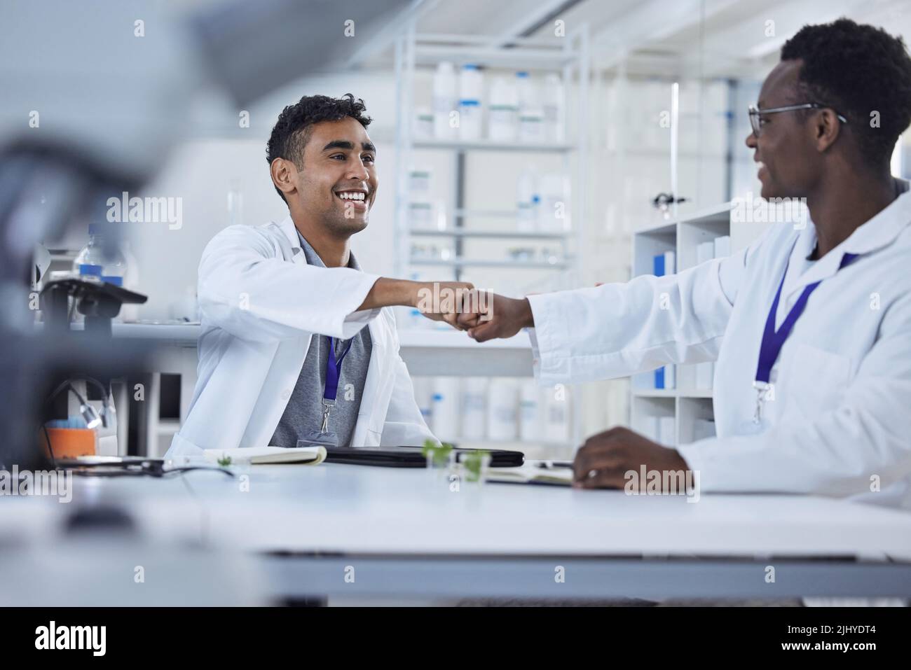 Two diverse mixed race professional scientist fist bumping and smiling ...