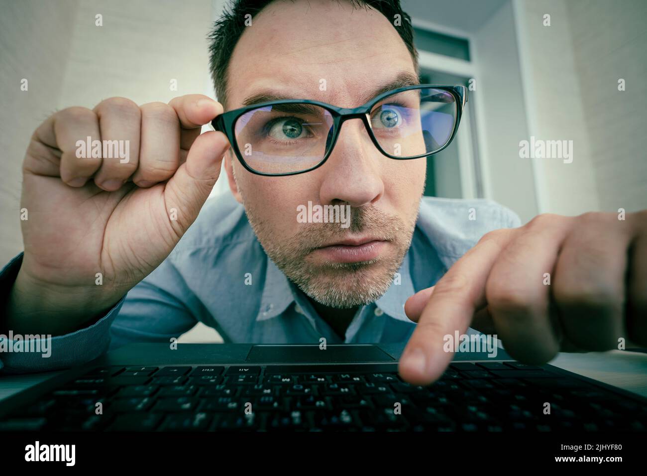 A young handsome man in a blue shirt is working at a computer on a ...