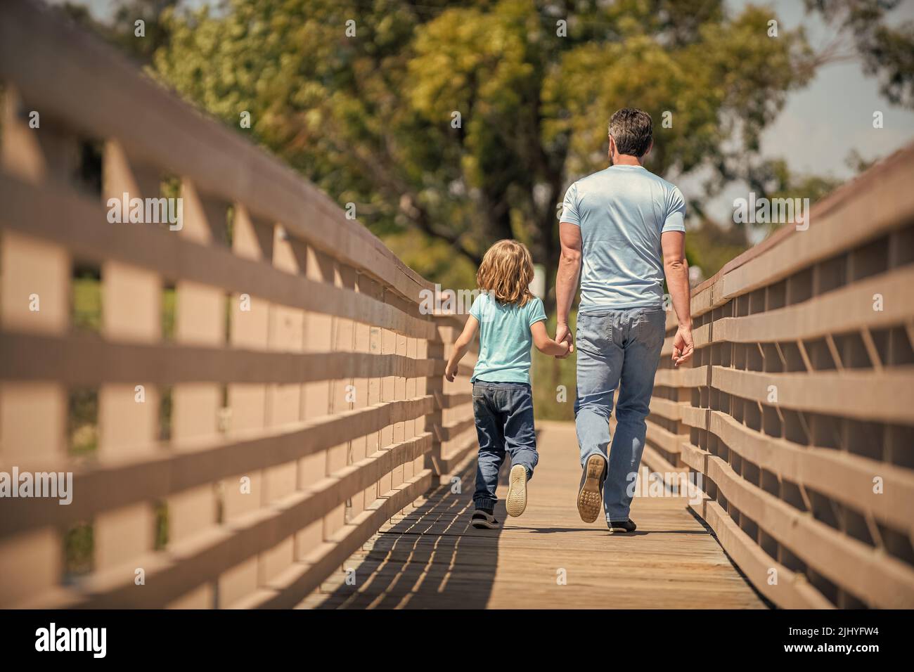 happy father leads with his kid walking outdoor, back view, parenting ...