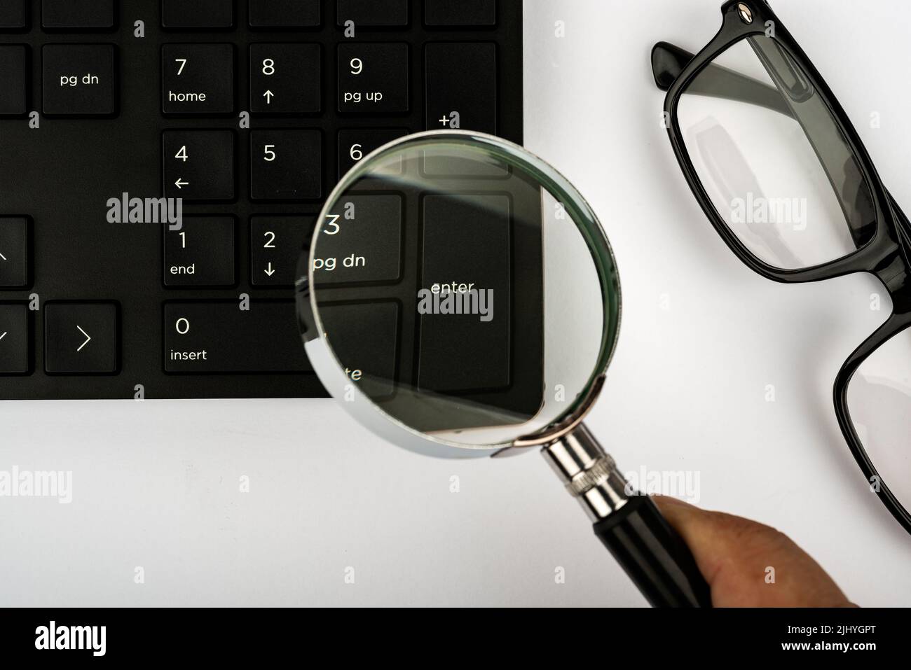 A part of a black computer keyboard, a magnifier and eyeglasses ...