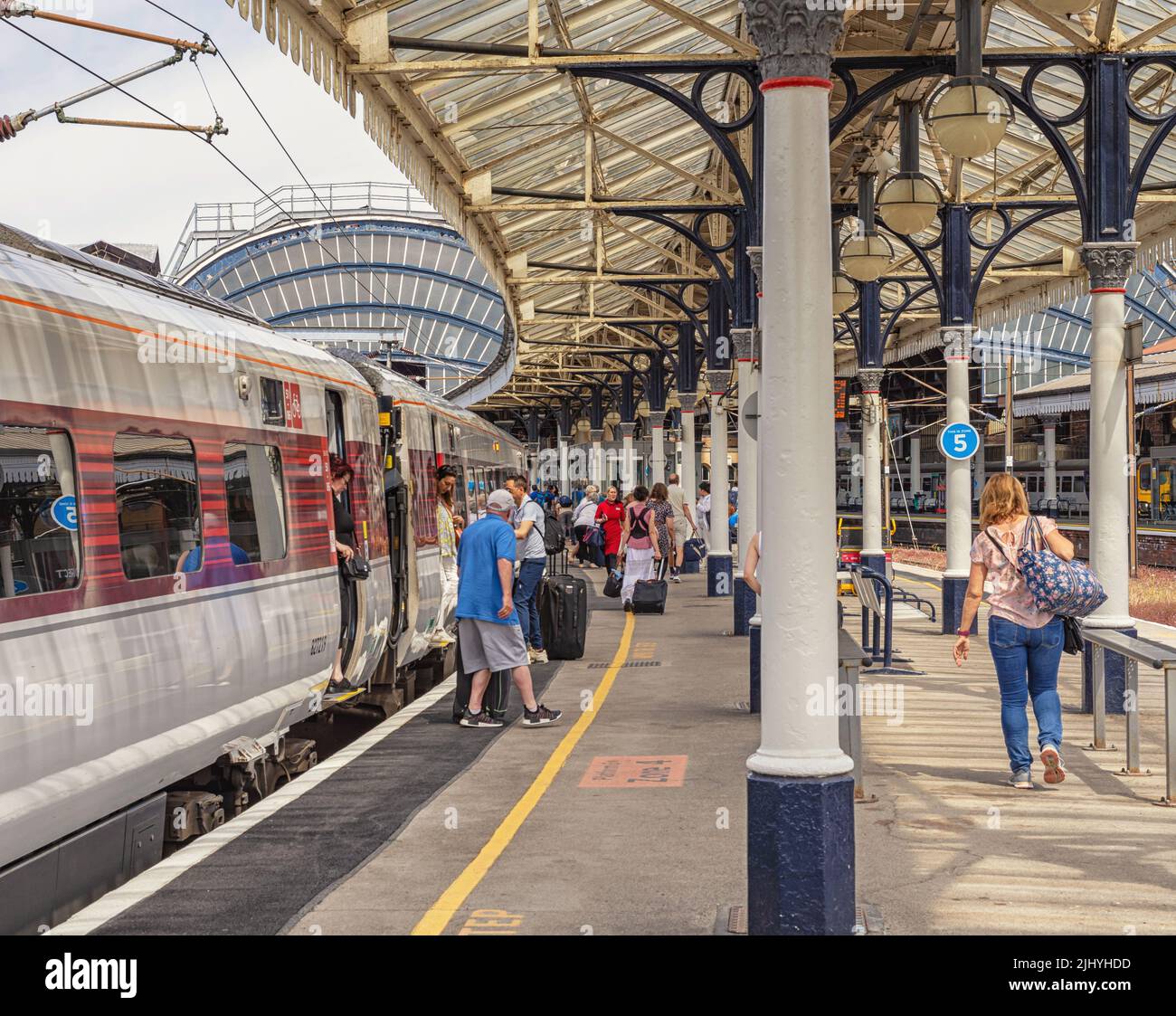 A train rests at a railway station platform and passengers alight from ...