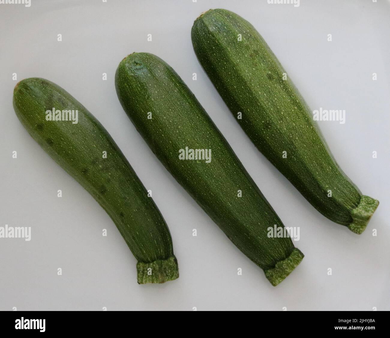 Three assorted green courgettes lying on a plain white background Stock ...