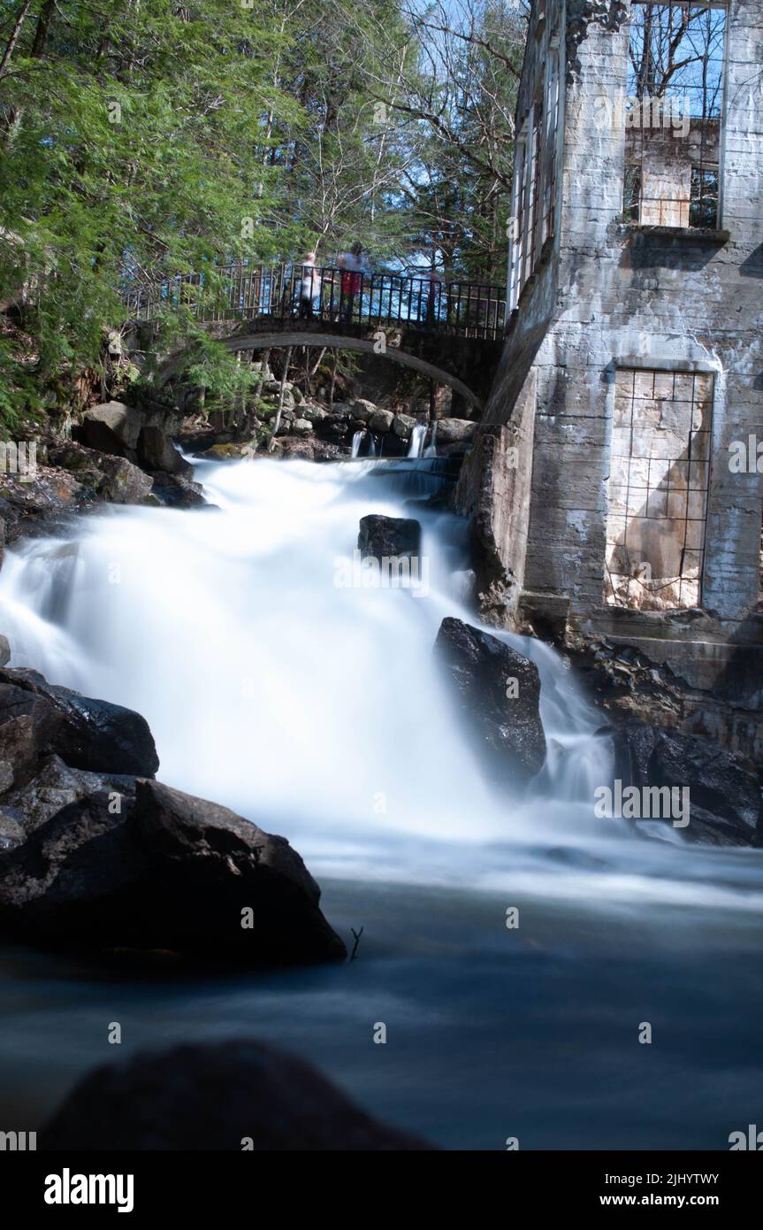 A vertical shot of an abandoned house next to a small waterfall with ...