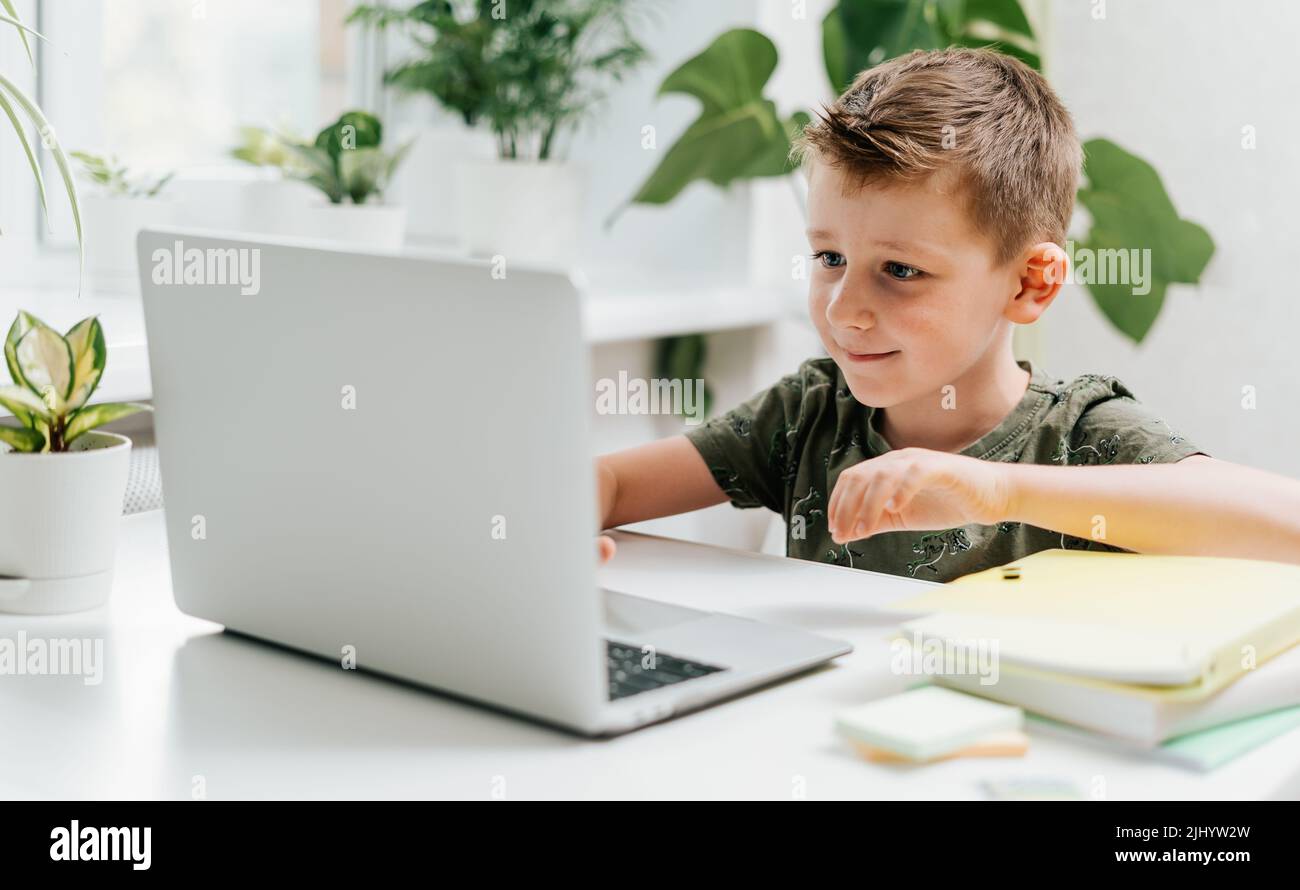Smile school kid boy studying at home with laptop and doing homework ...