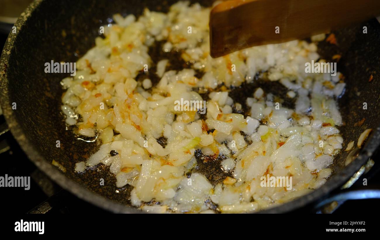 cooking and mixing fried onions by wooden spoon in a pan with sunflower ...