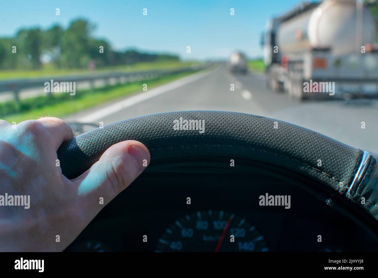 driver hand on the wheel of a car that is driving along the highway ...