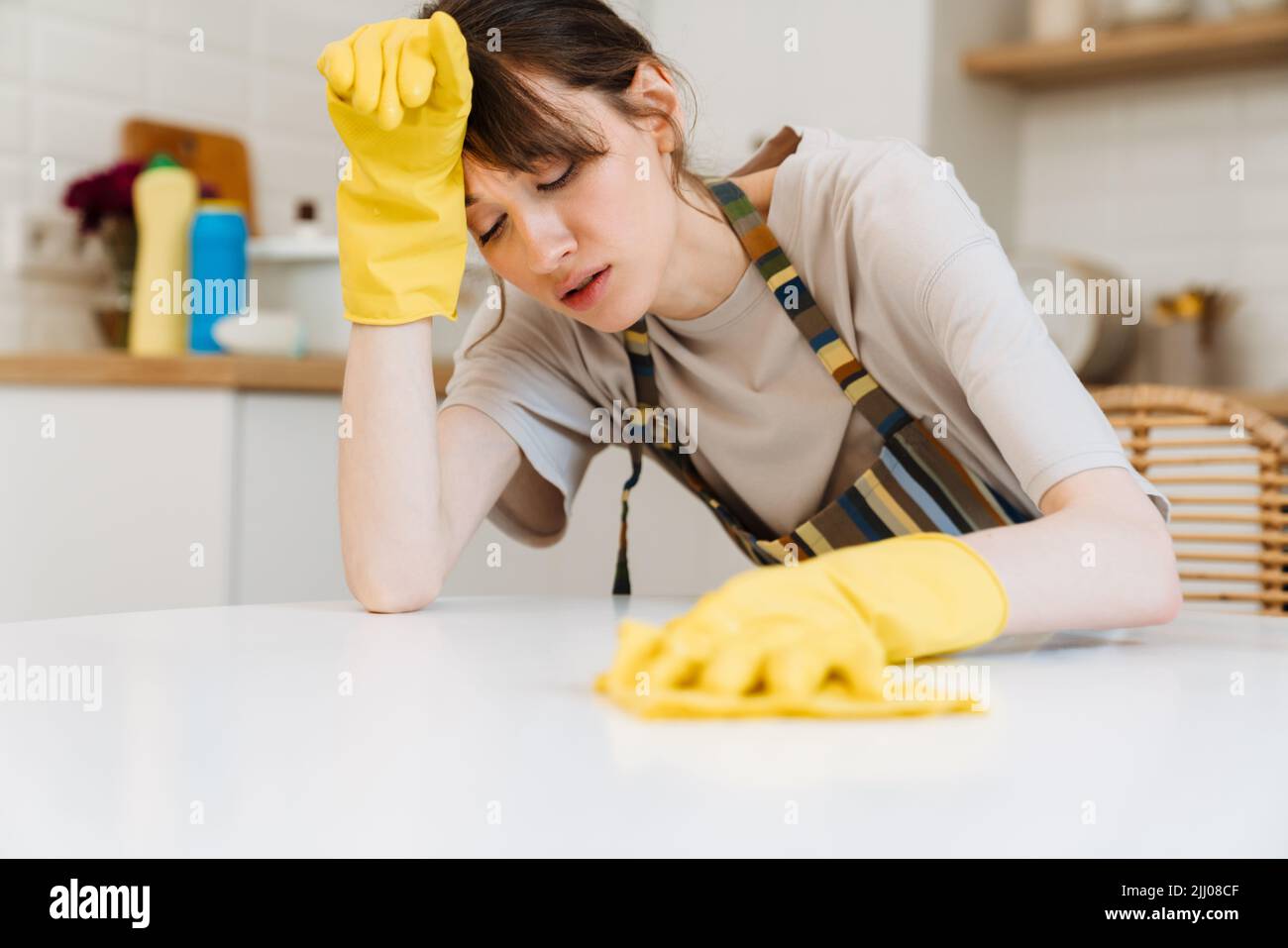 White young woman in gloves wiping her forehead while cleaning table at ...