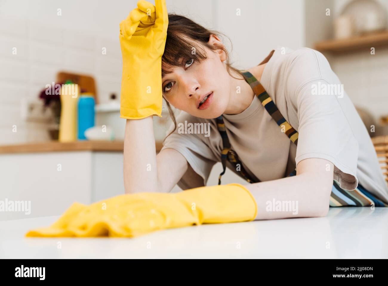 White young woman in gloves wiping her forehead while cleaning table at ...