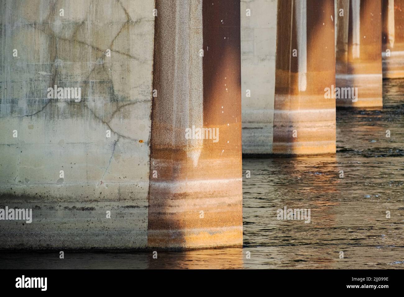Under a commuter bridge with pillars in water on a sunny summer morning ...