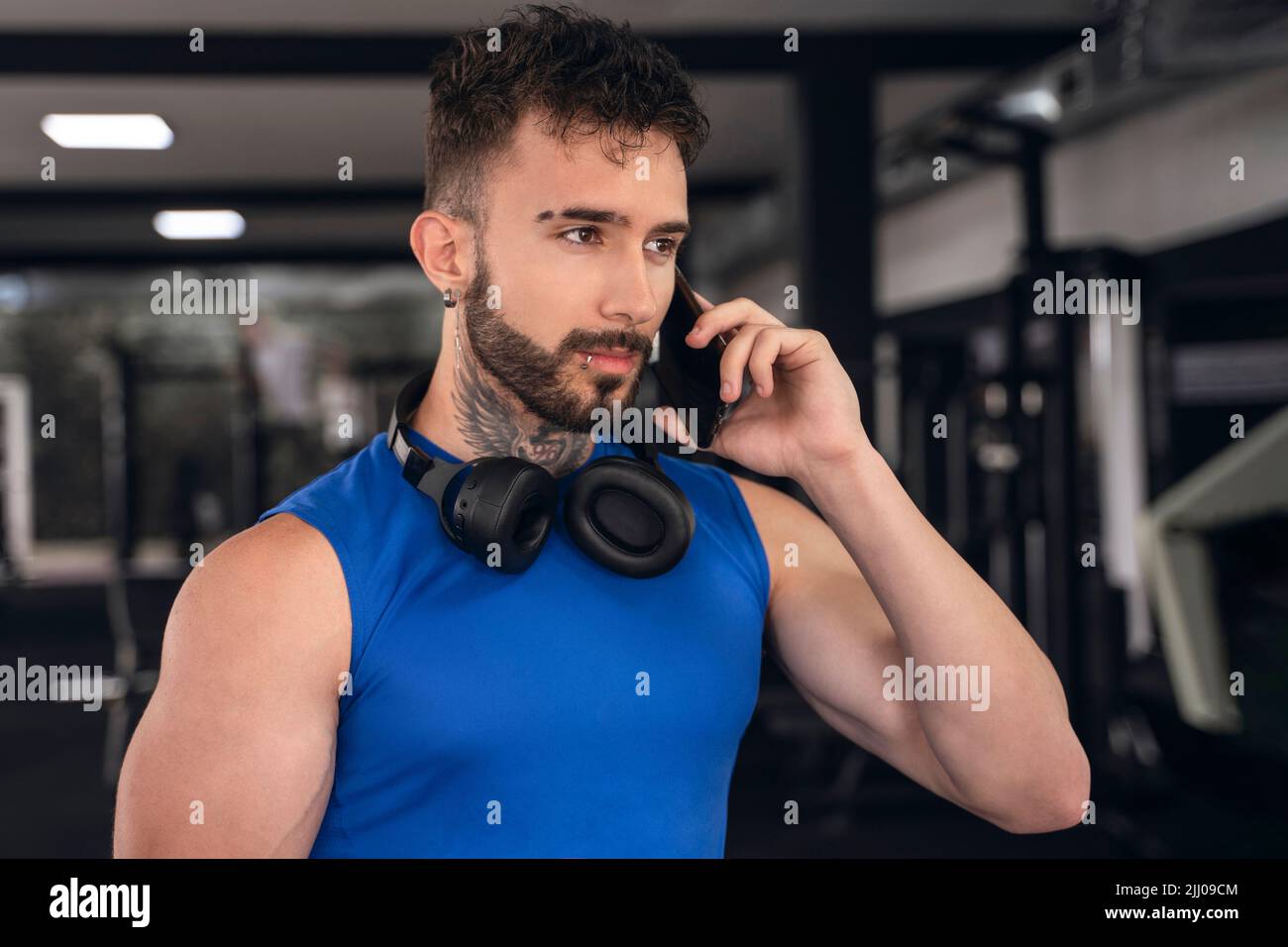 Handsome male with tattoos in his 20s talking on the phone in the gym ...