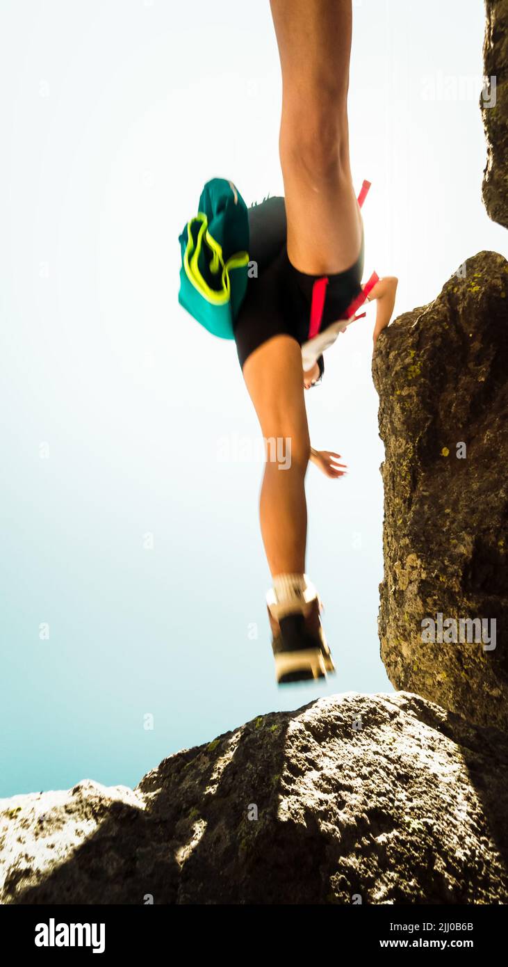 Low view female body step feet in air on hiking over rocks outdoors ...