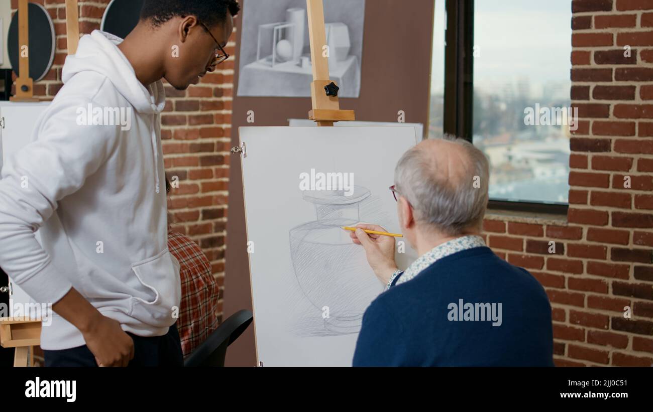 Young artist explaining drawing technique to elder person, using pencil ...