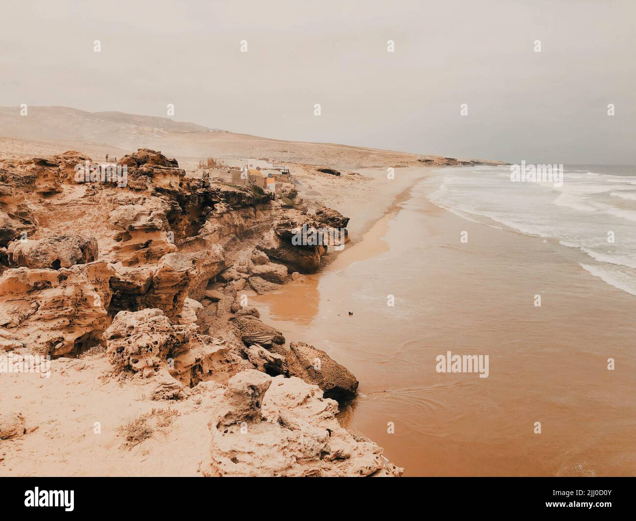 A stormy sea waving near a sandy shore surrounded by rocks Stock Photo ...