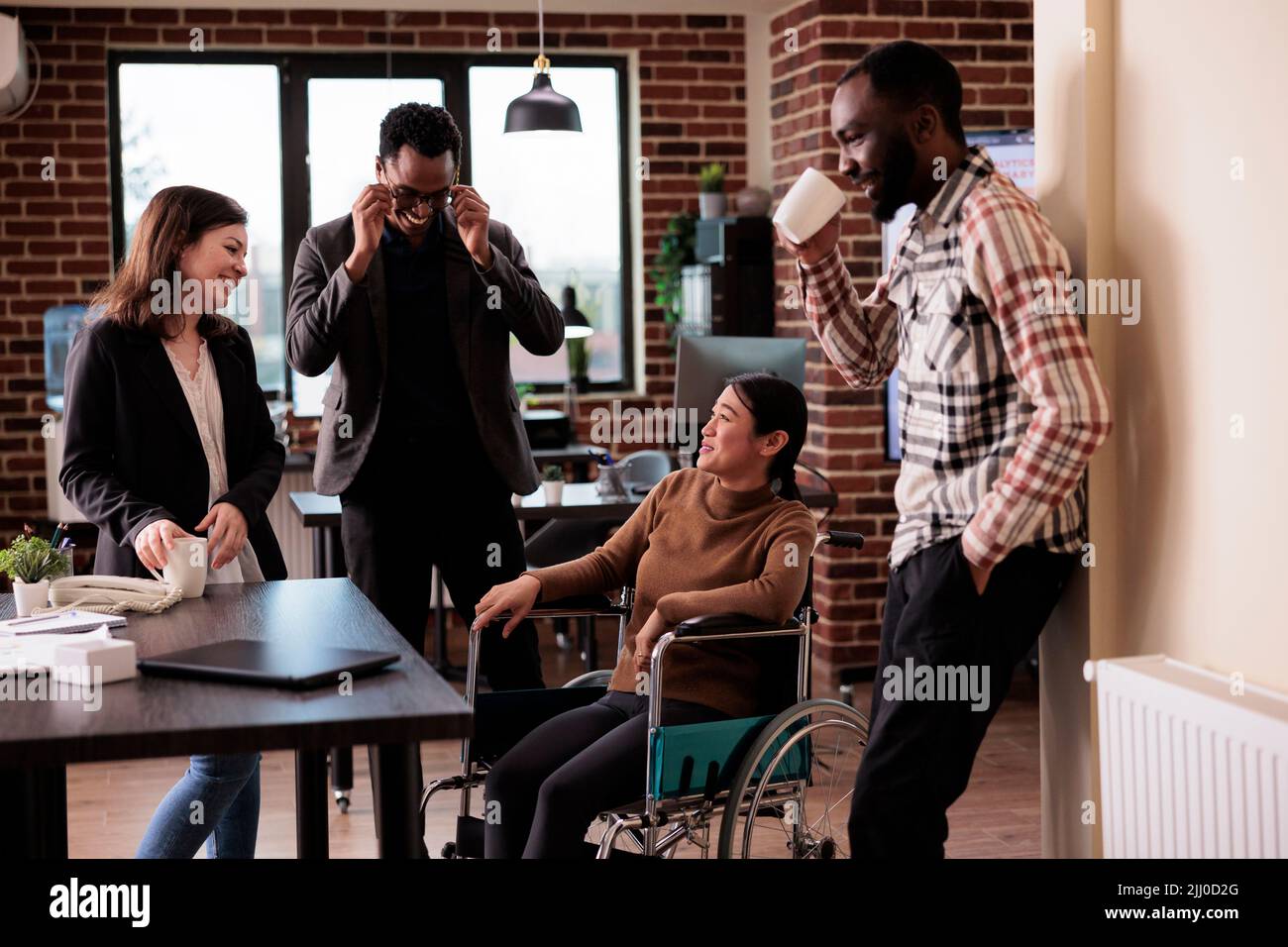 Diverse team of colleagues laughing in business office with paralyzed ...