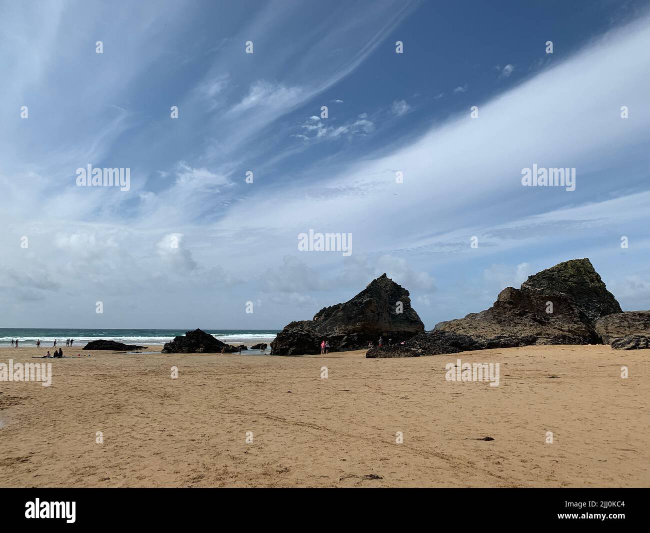 A sandy beach with huge black rocks under a blue cloudy sky with long ...