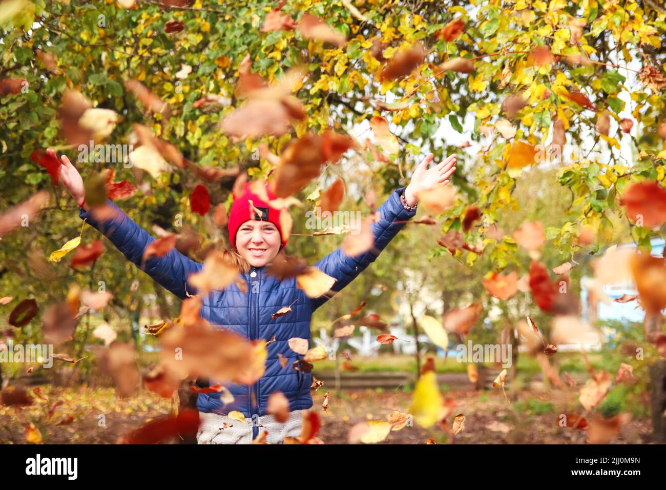 Defocus autumn people. Teen girl raising hand and throwing leaves. Many ...