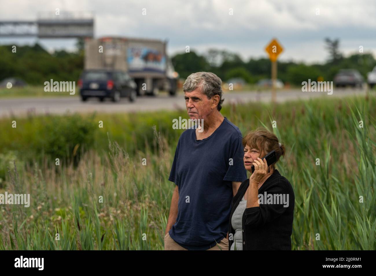 A couple looks at a procession of motorcycles along the highway ...