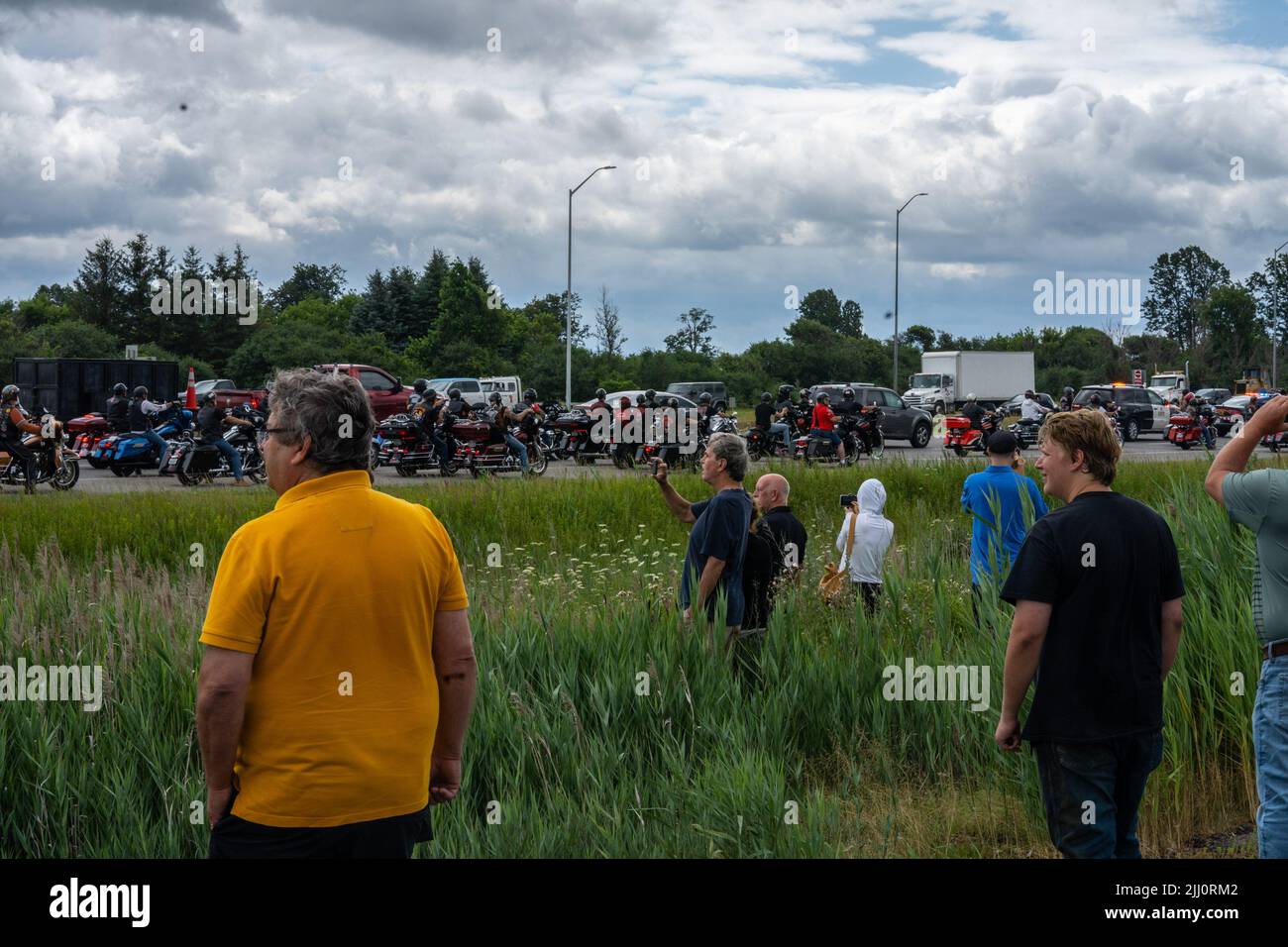 People look at a procession of motorcycles along the highway. Hundreds ...