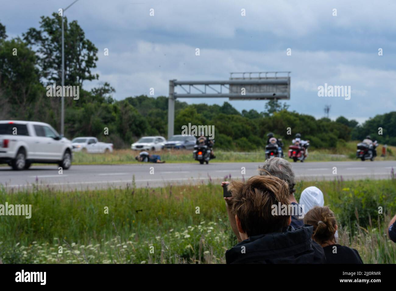 People look at a procession of motorcycles along the highway. Hundreds ...
