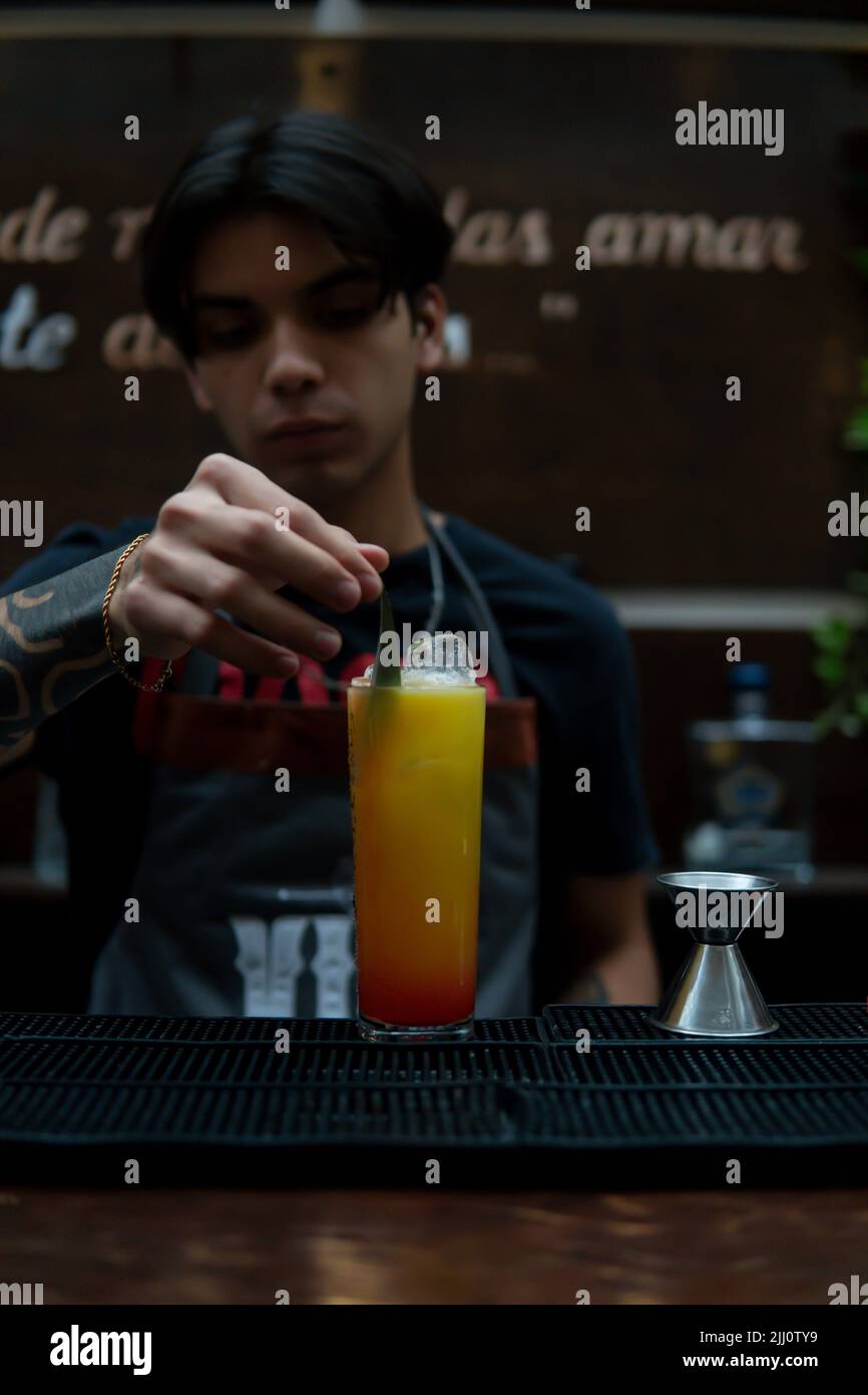 Waiter preparing a yellow drink that looks like juice, he is placing a ...