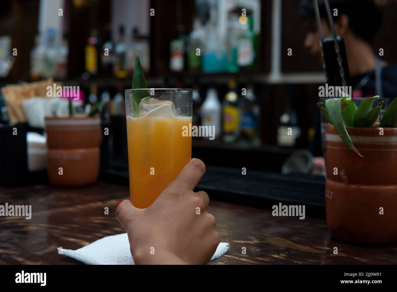 Hand of a girl drinking a yellow drink at the bar counter. Close up to ...