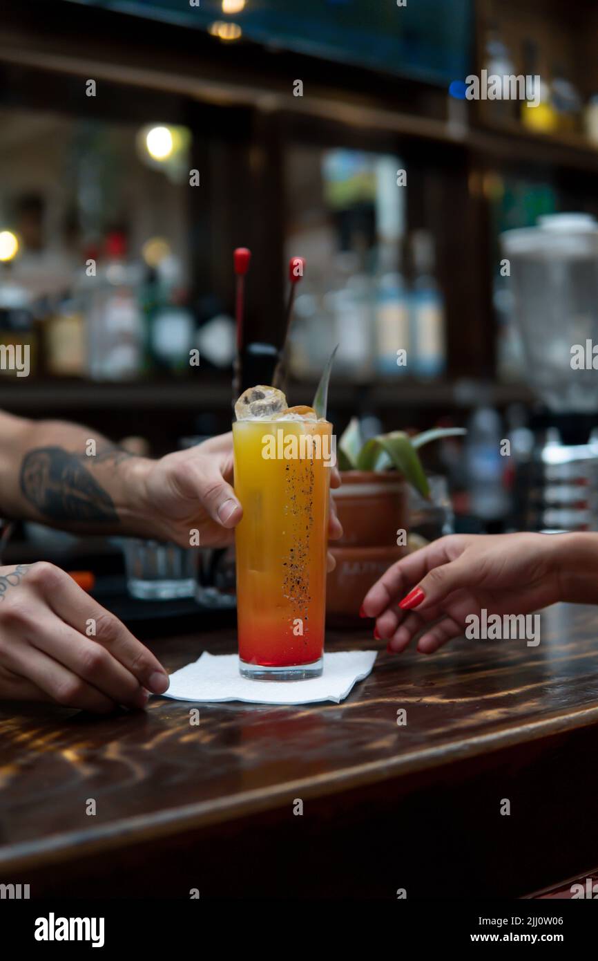 Bartender handing a yellow drink to a girl. They meet in a bar or ...