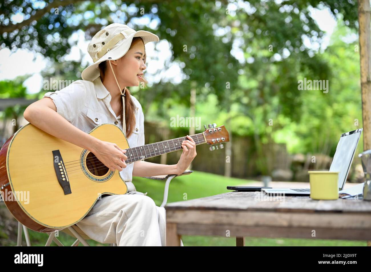 Relaxed and happy young Asian woman sing a song while playing guitar ...