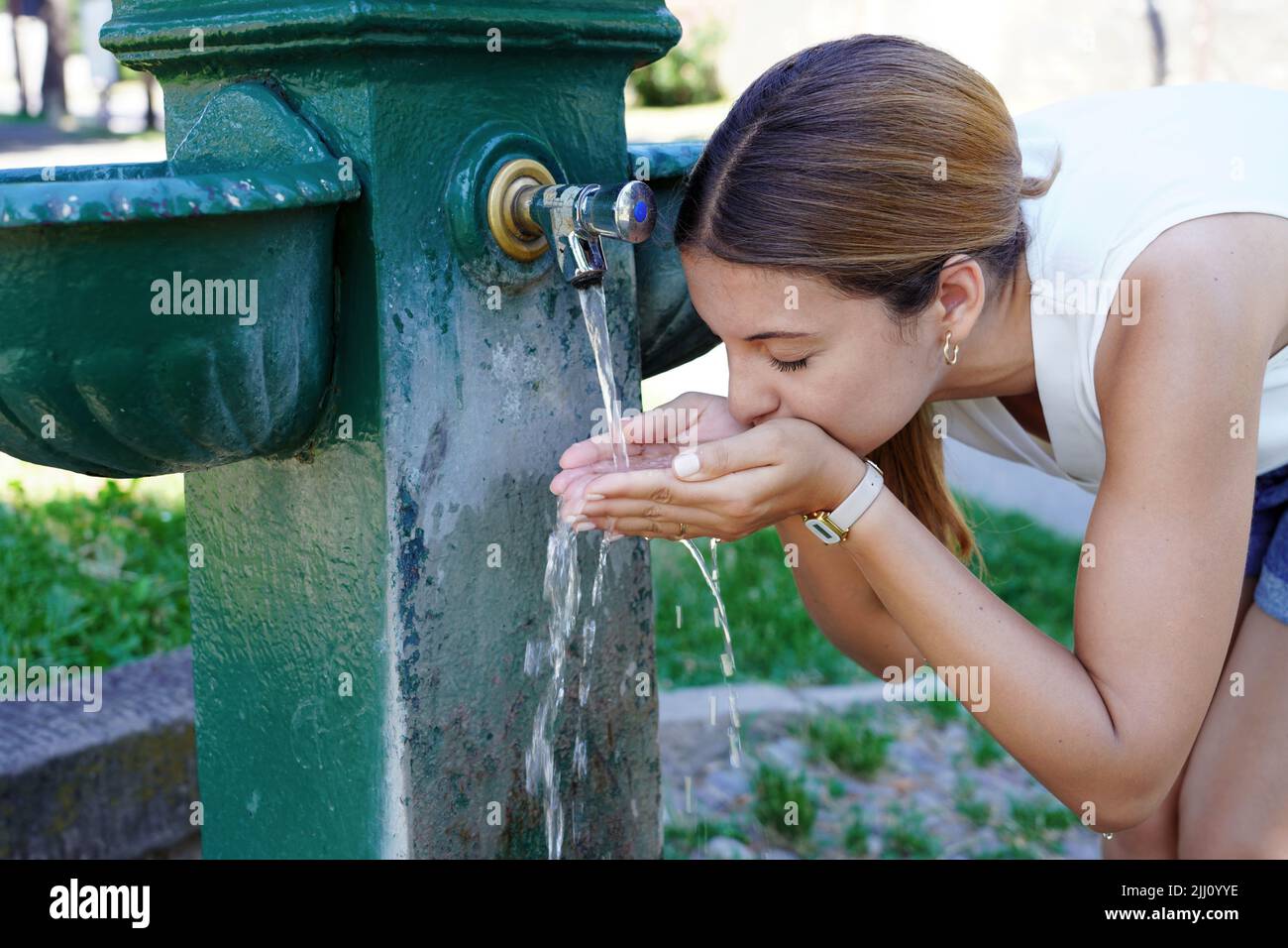 Water shortage emergency. Young woman hydrates herself from a fountain ...