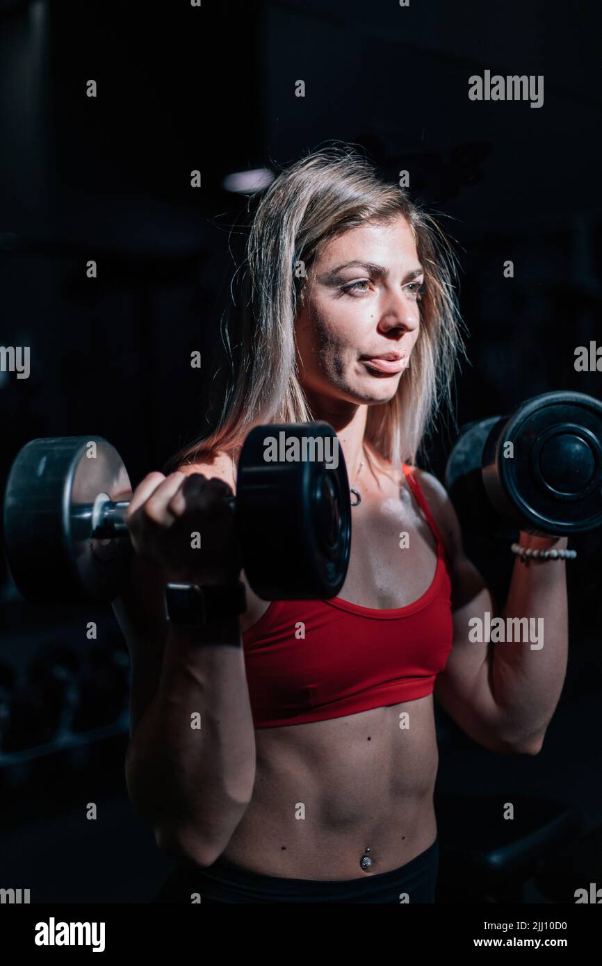 fit woman using dumbbells in dark gym with sun on her face Stock Photo ...