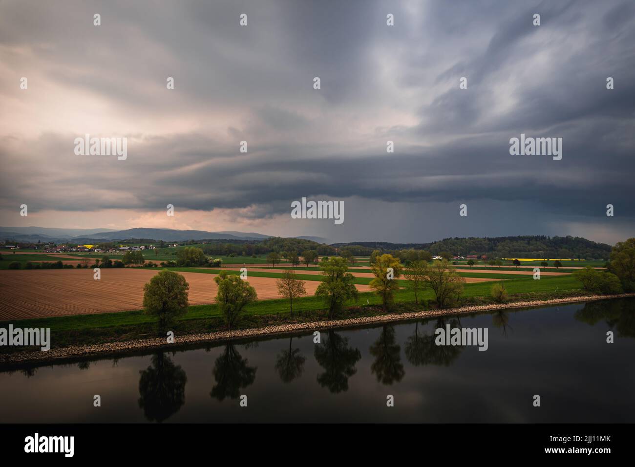 A beautiful view of a lake and a field with trees under the cloudy sky ...