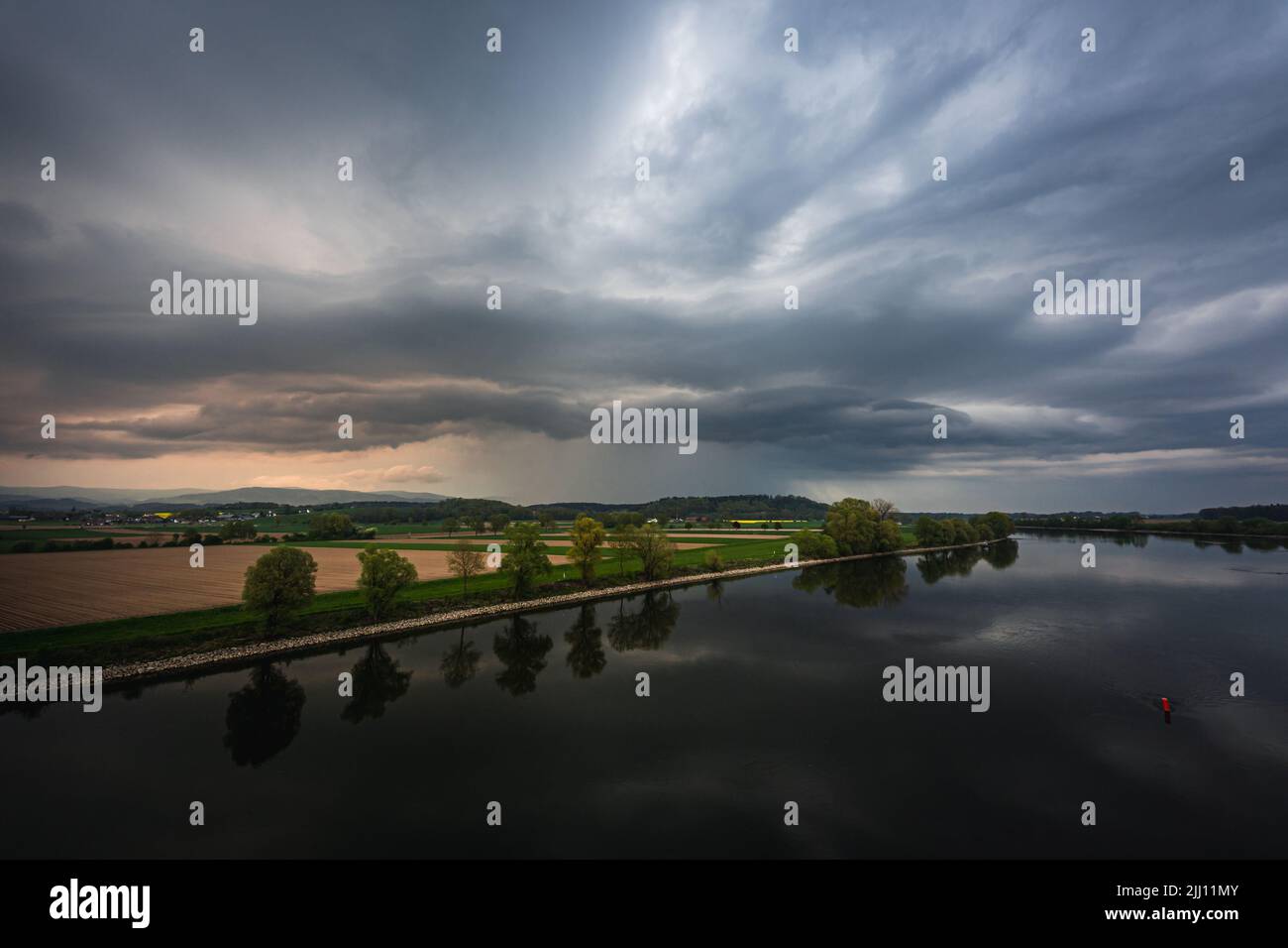 A beautiful view of a lake and a field with trees under the cloudy sky ...