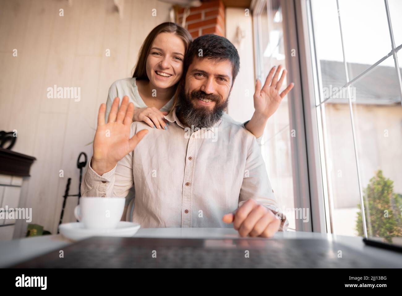 Happy young european couple resting at living room, waving hand hello ...
