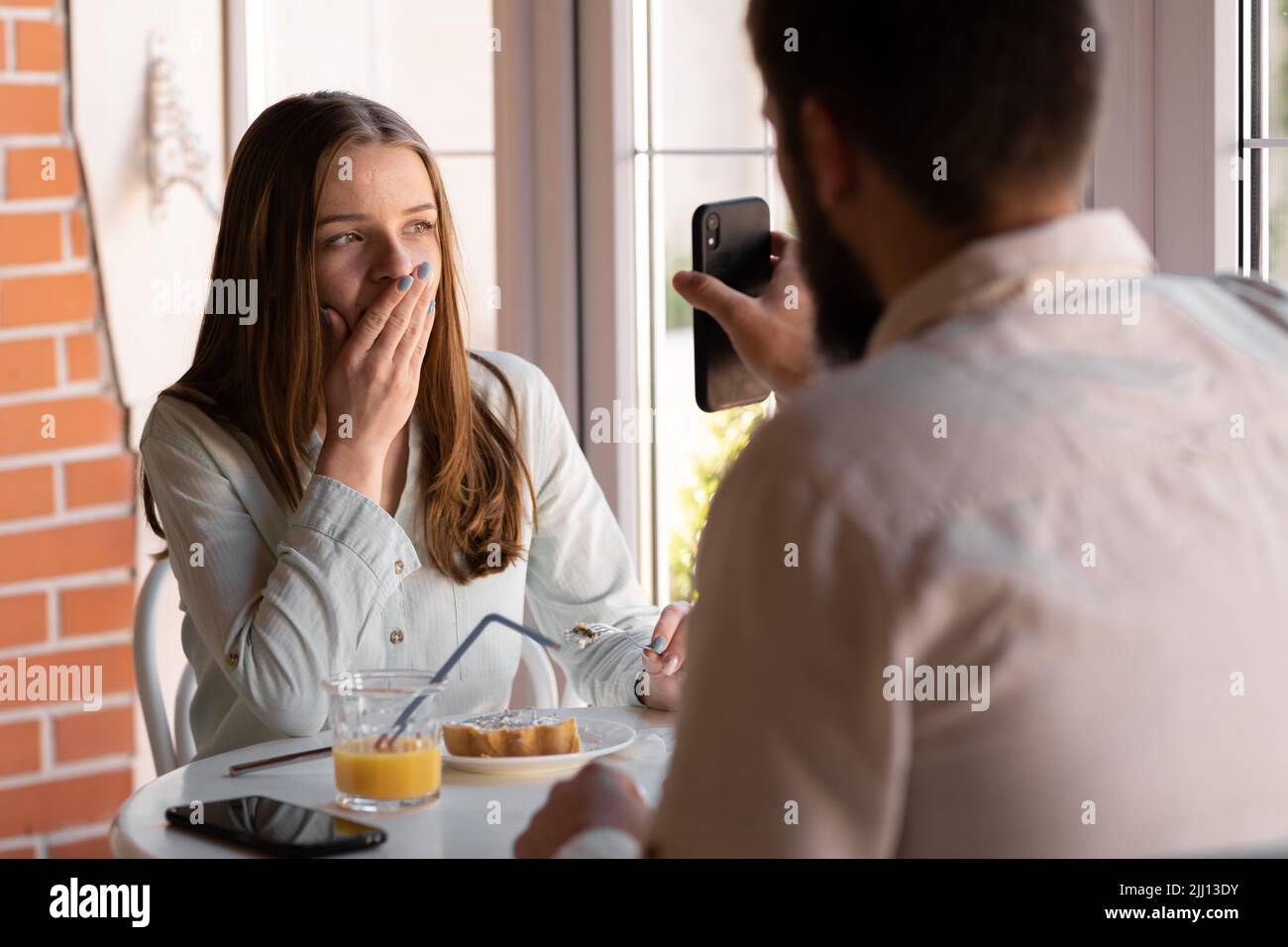 couple enjoy breakfast in cafe, man shows smartphone screen to woman ...